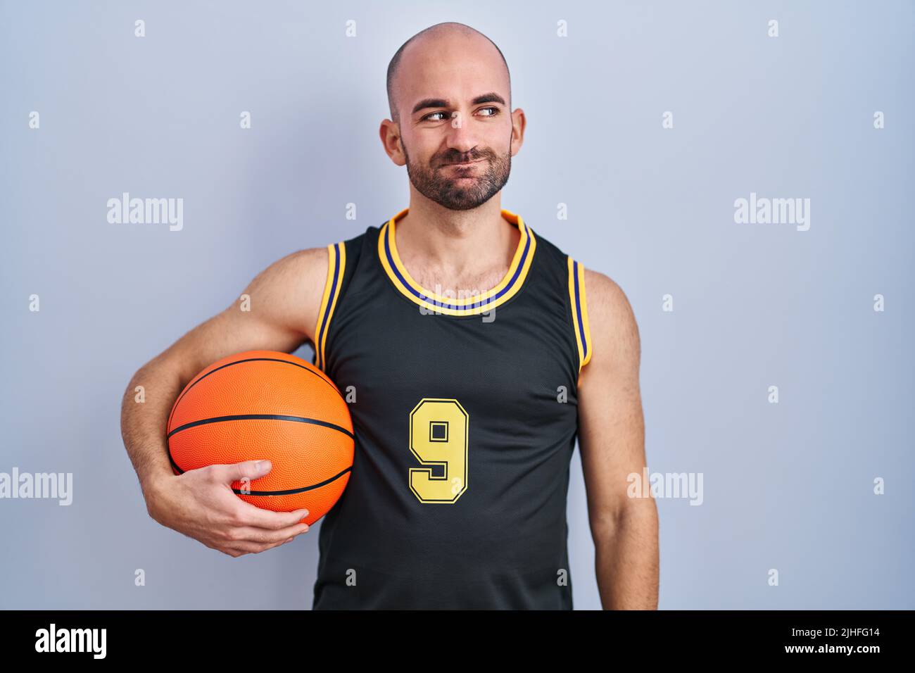 Young bald man with beard wearing basketball uniform holding ball ...