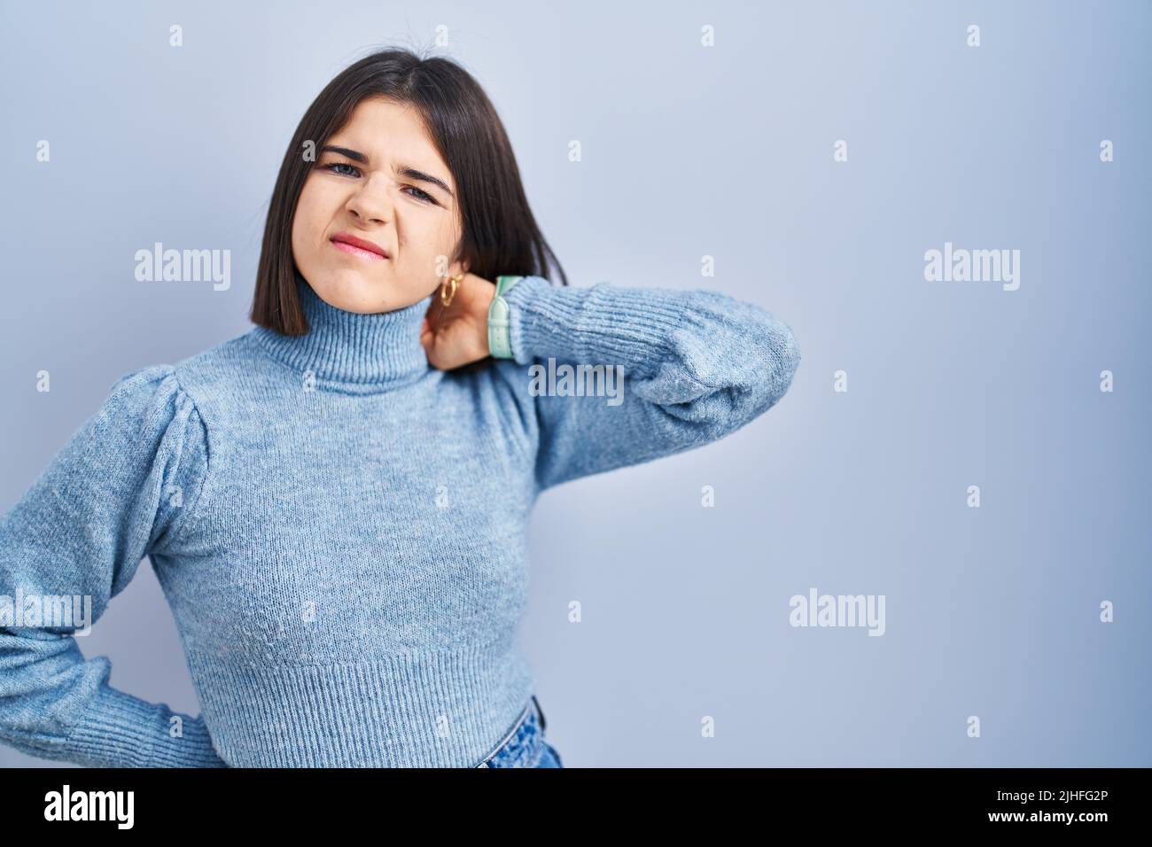 Young hispanic woman standing over blue background suffering of neck ...
