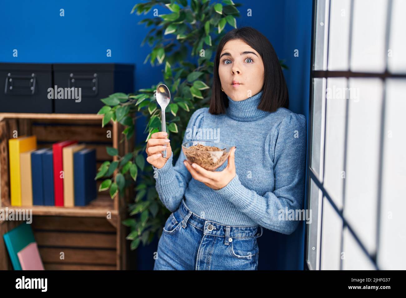 Young hispanic woman eating healthy whole grain cereals with spoon ...