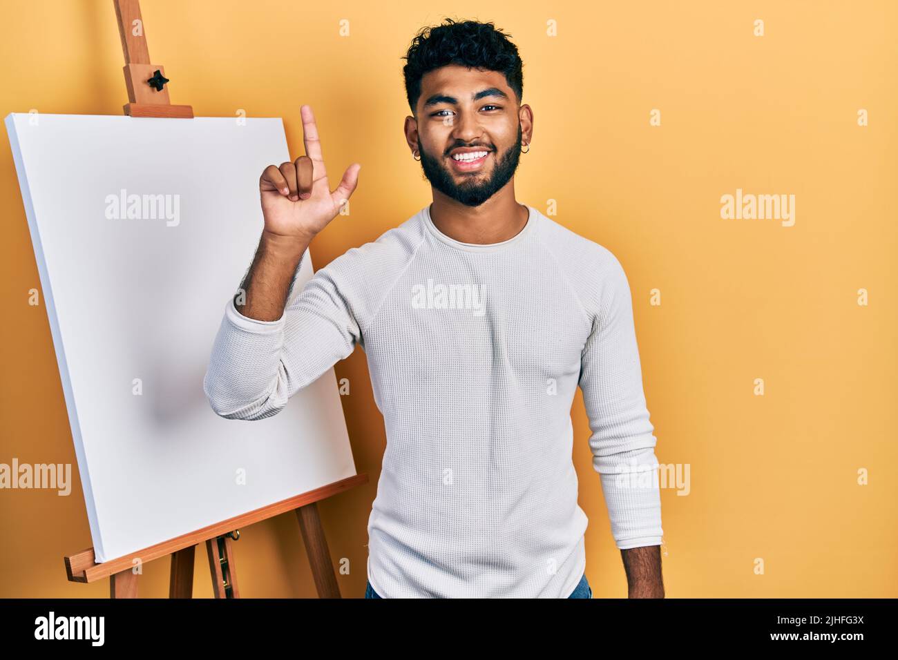 Arab man with beard standing by painter easel stand smiling with an ...