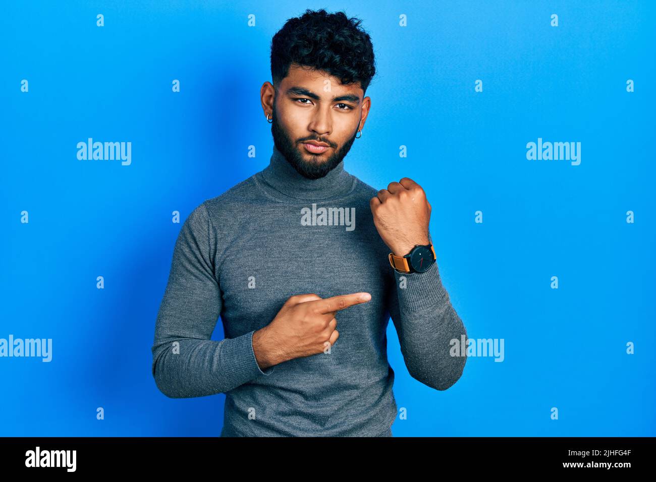 Arab man with beard wearing turtleneck sweater in hurry pointing to ...