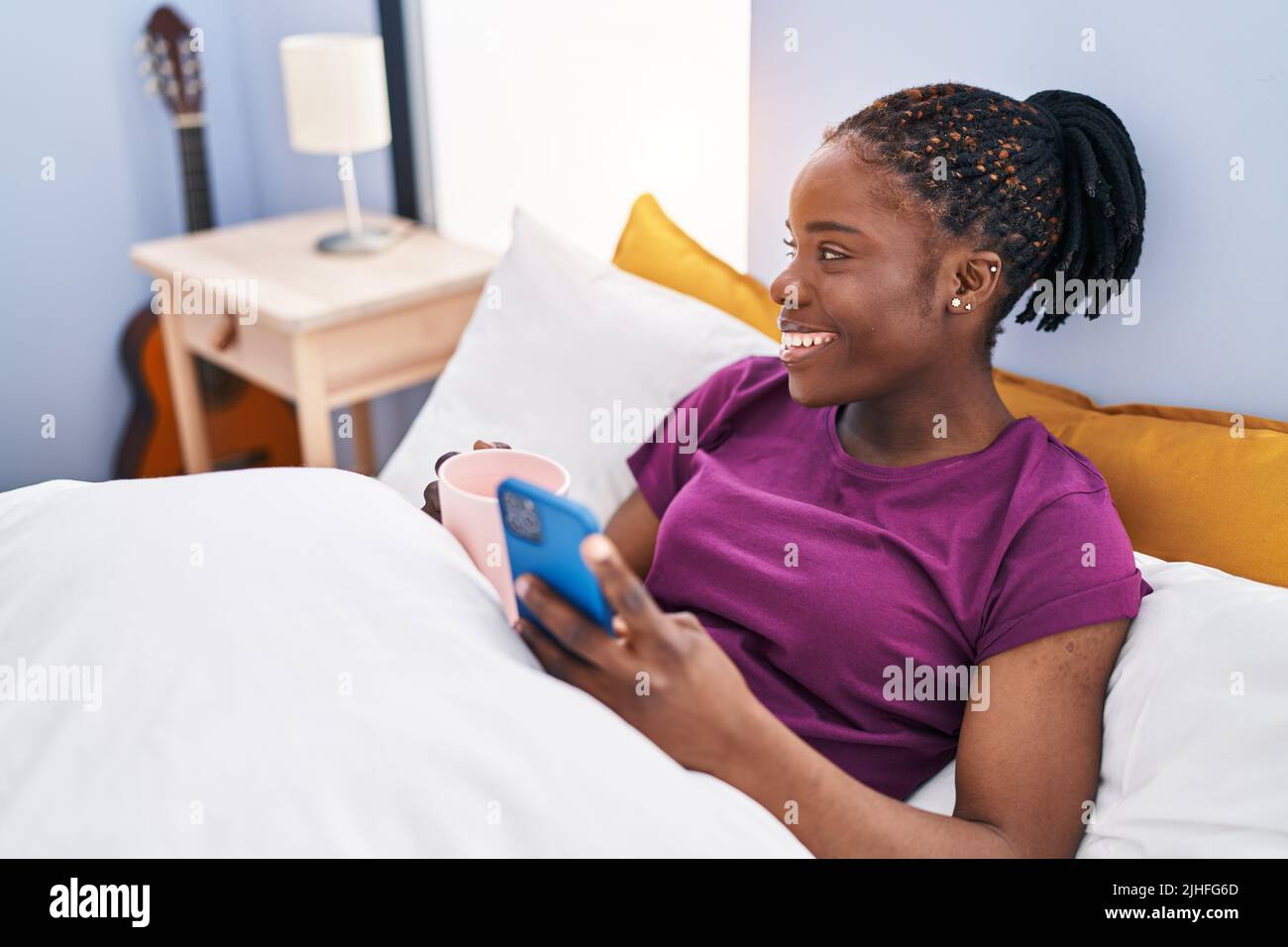 African american woman using smartphone and drinking coffee lying on ...