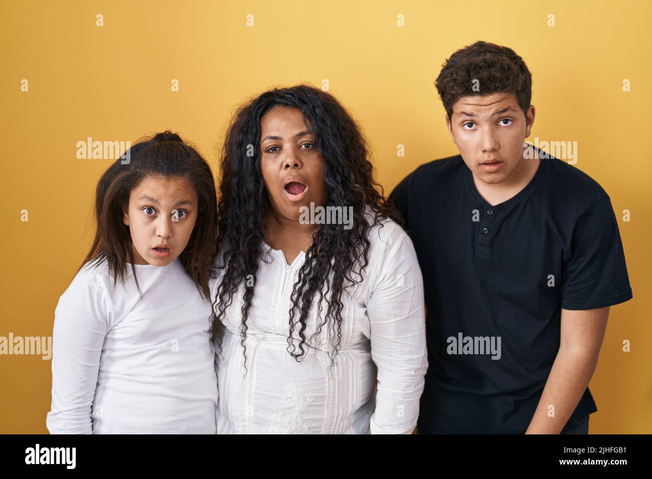 Family of mother, daughter and son standing over yellow background in ...