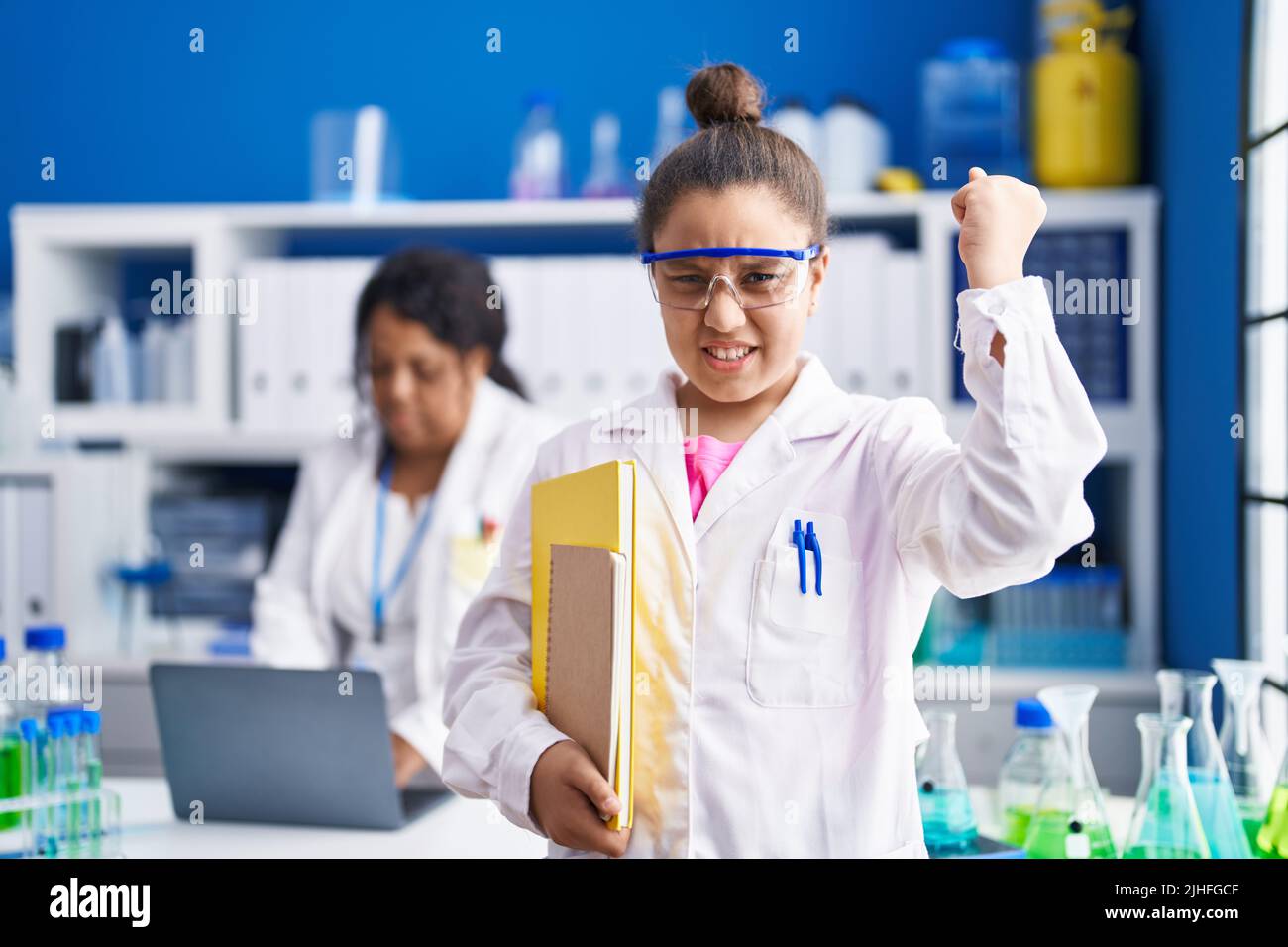Mother and young daughter working at scientist laboratory annoyed and ...
