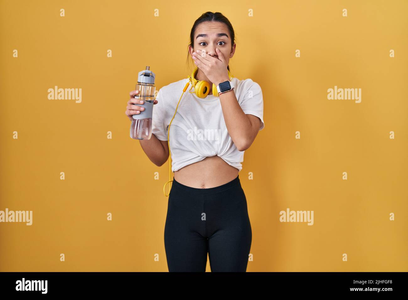 Young south asian woman wearing sportswear drinking water shocked ...
