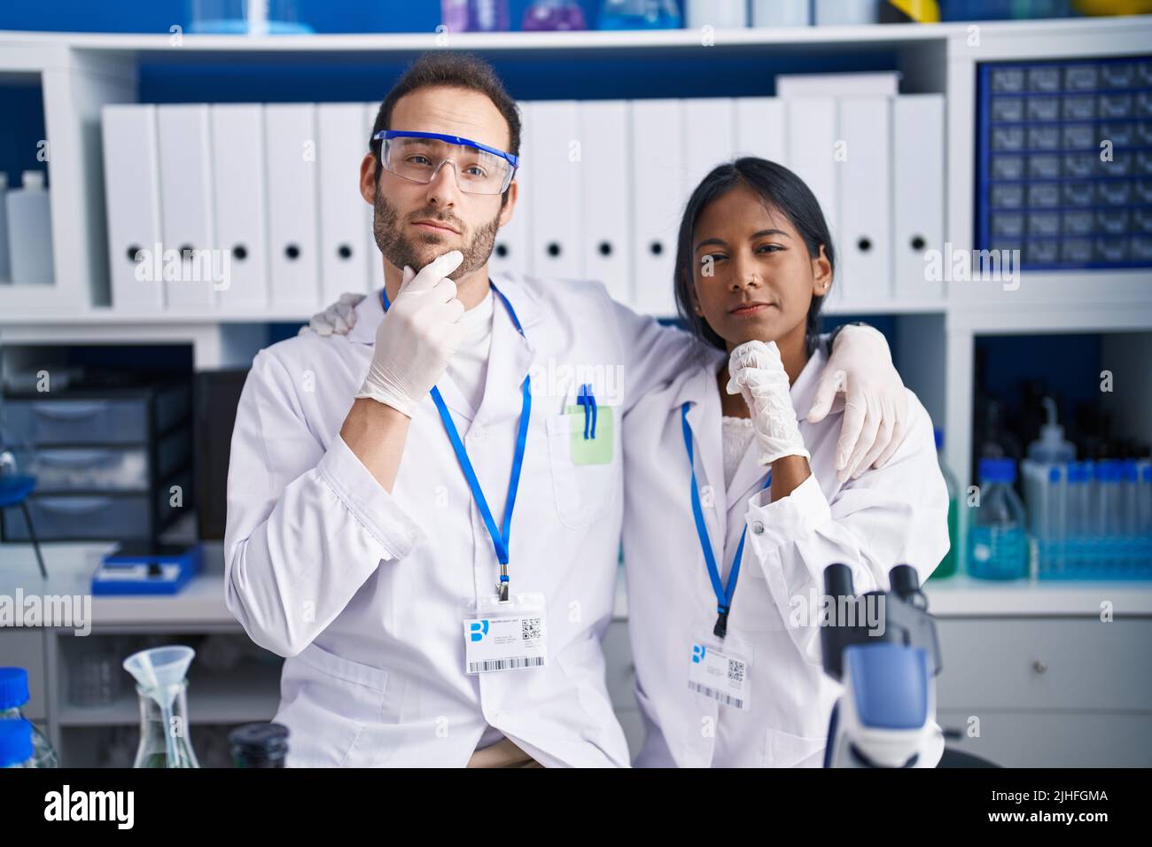 Interracial couple working at scientist laboratory serious face ...