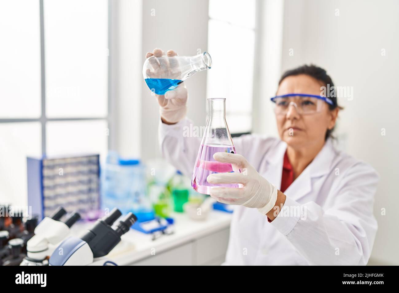 Middle age hispanic woman wearing scientist measuring liquid at ...