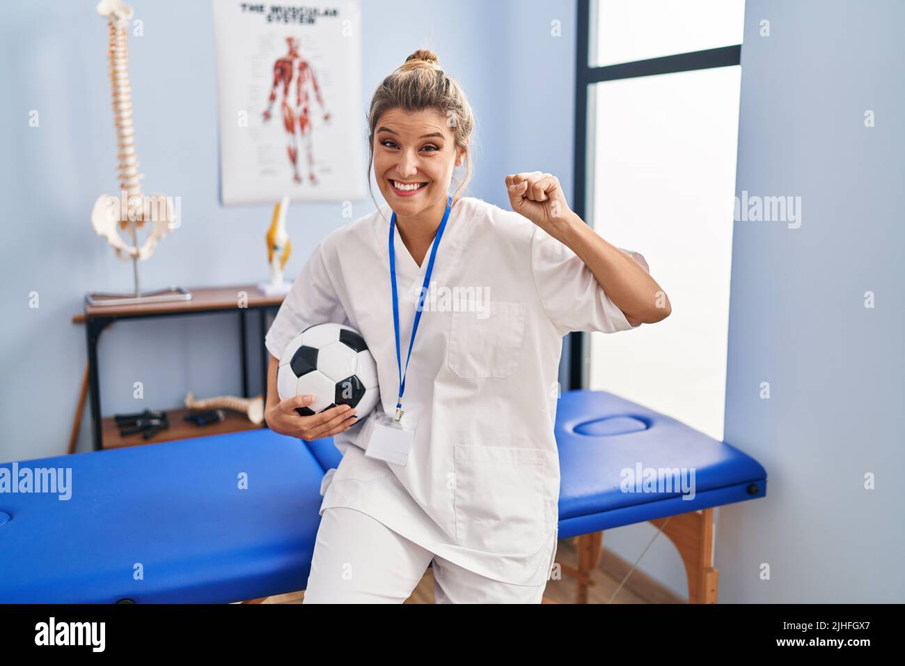 Young woman working at football therapy clinic screaming proud ...