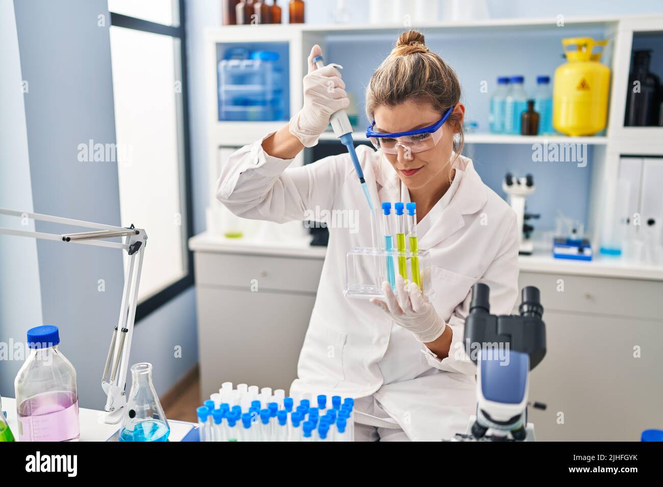 Young blonde woman wearing scientist uniform using pipette at ...