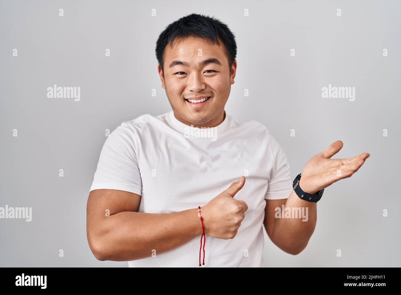 Young chinese man standing over white background showing palm hand and ...