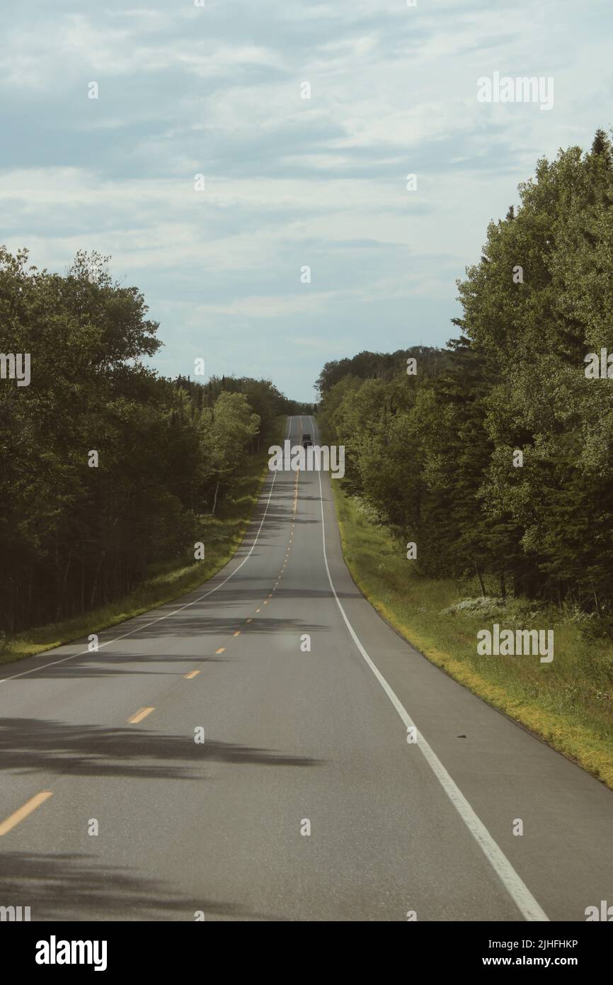 Tar Road Lined with Green trees and grass. Ascending up hill. Blue sky ...