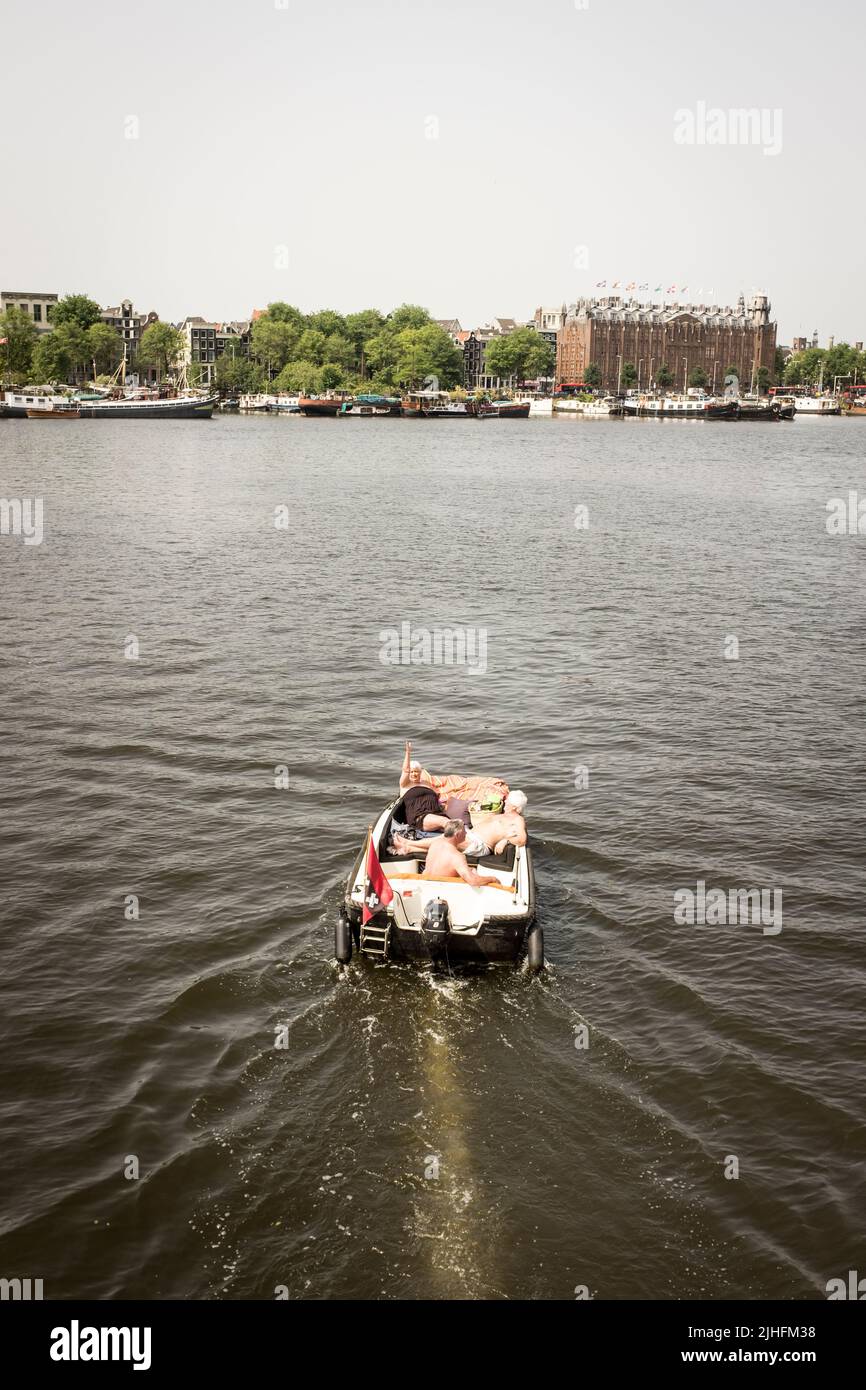 People enjoy the sun in a small motorboat on the canal on a hot and ...
