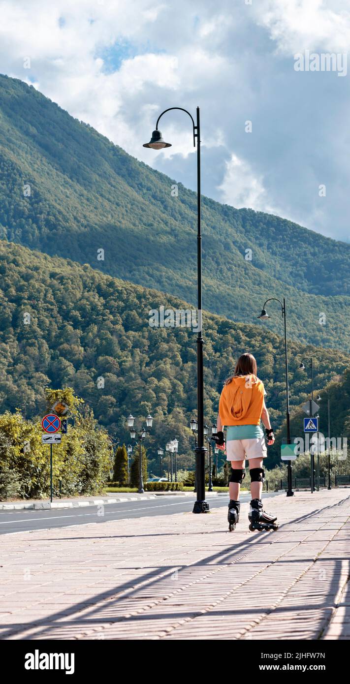 rear view of Young blond woman in protective equipment riding on roller ...