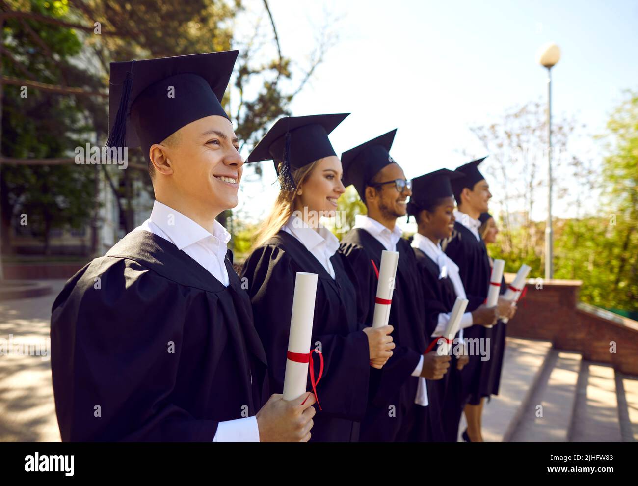 Happy multiracial graduates in student gown stand in row during ...