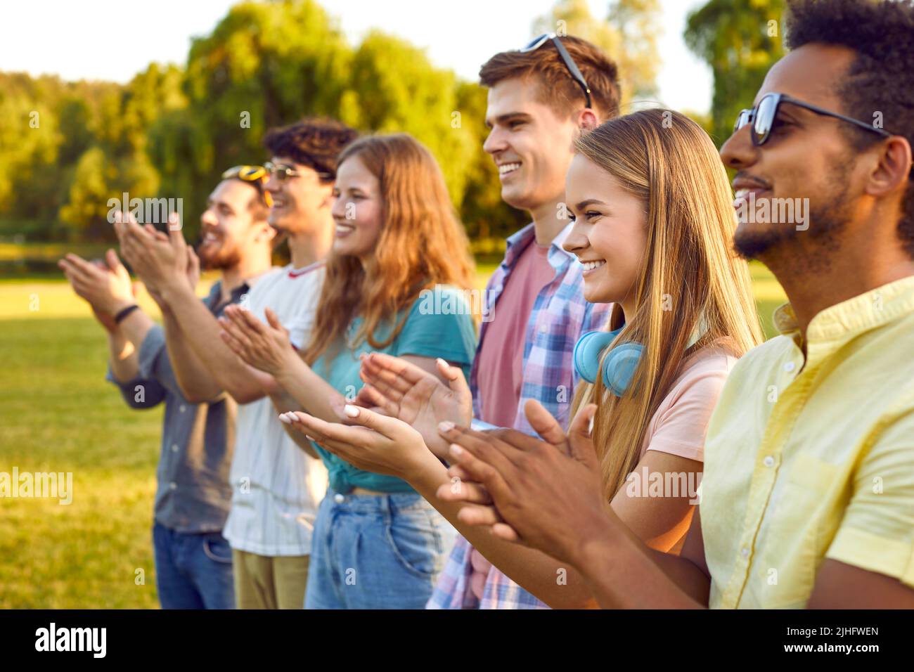 Diverse group of happy young people clapping hands at an outdoor summer ...