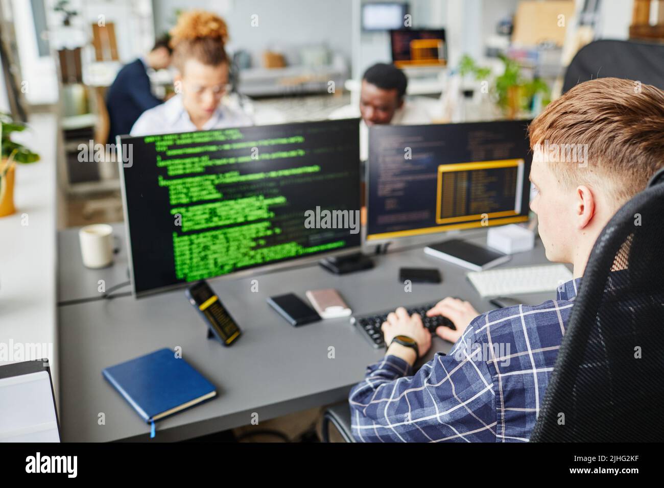 Rear view of young IT specialist writing codes of software sitting at ...