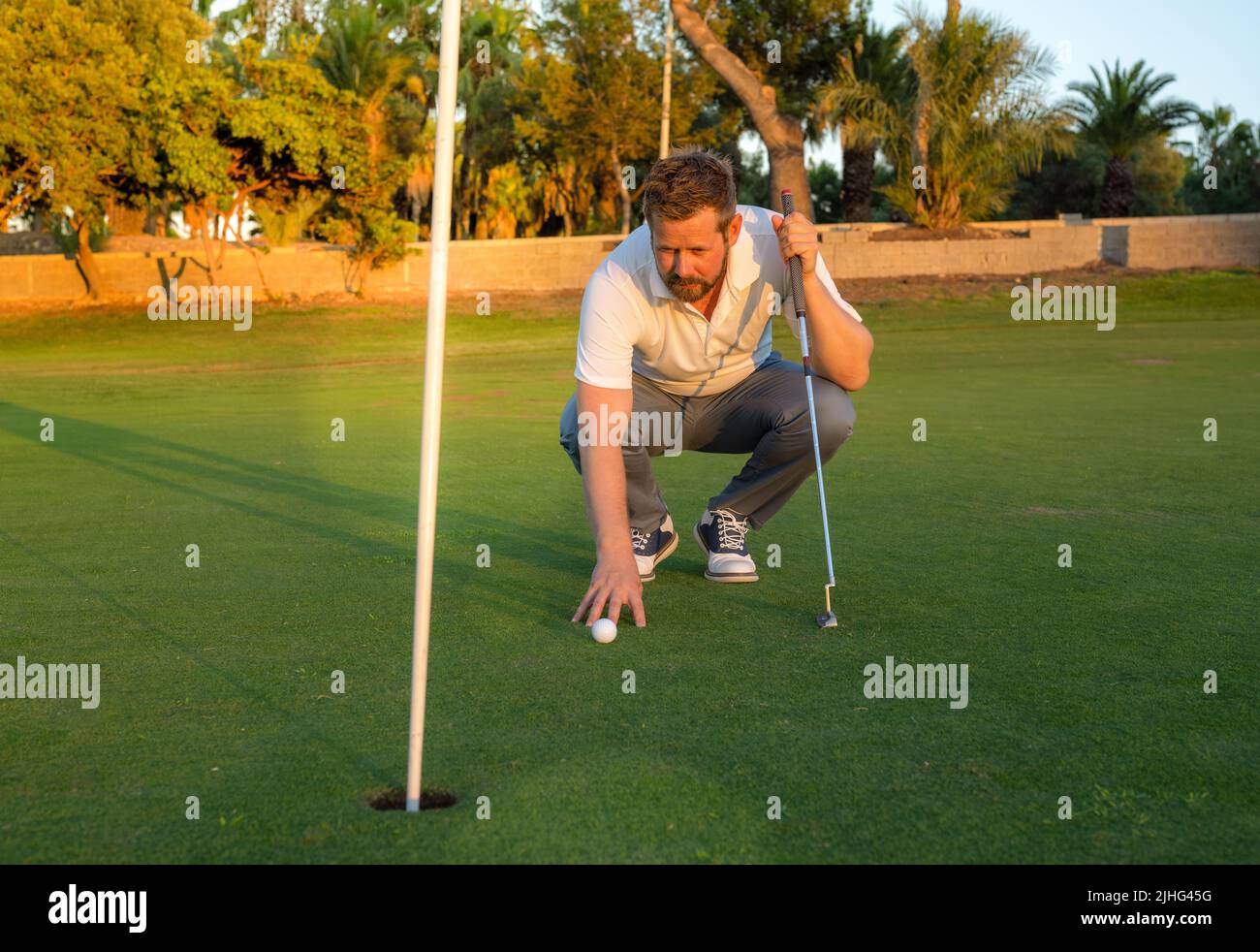 Pro golf player aiming shot with club on course. Male golfer on putting ...