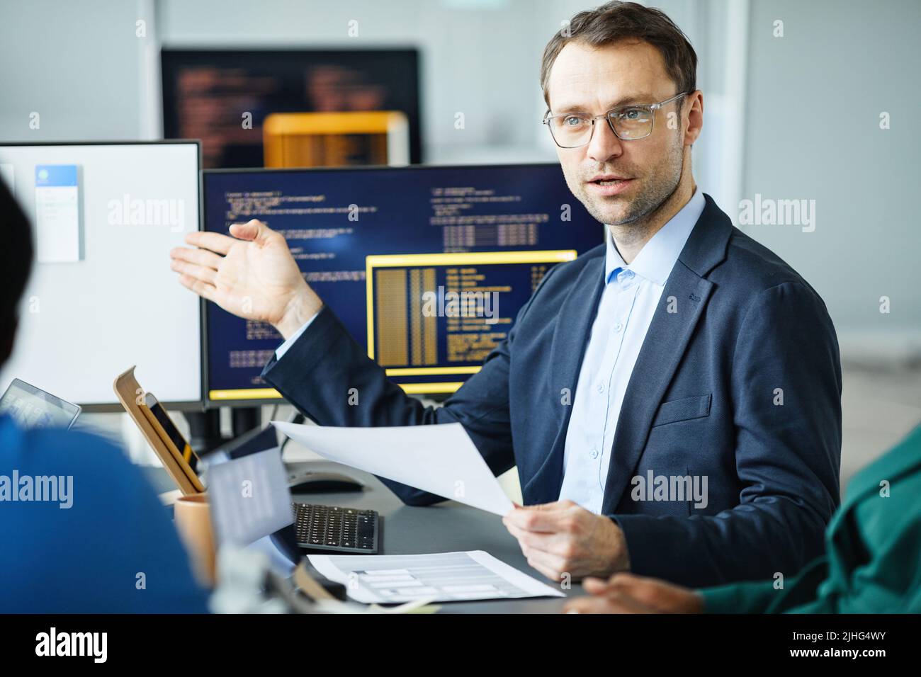 Mature developer pointing at computer monitor with interface and giving ...