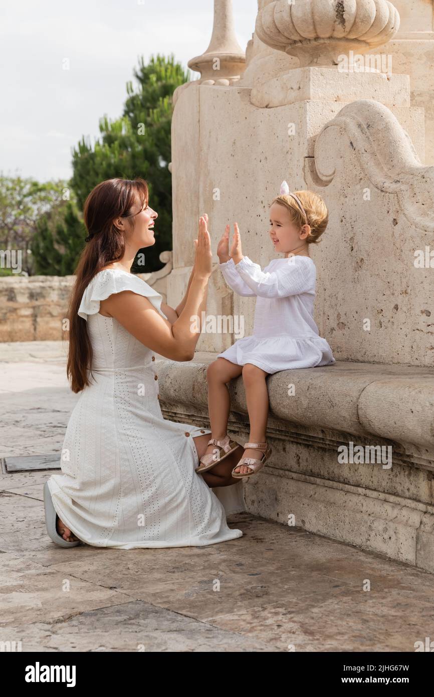 Smiling toddler kid playing patty cake game with mom on stone bench of ...