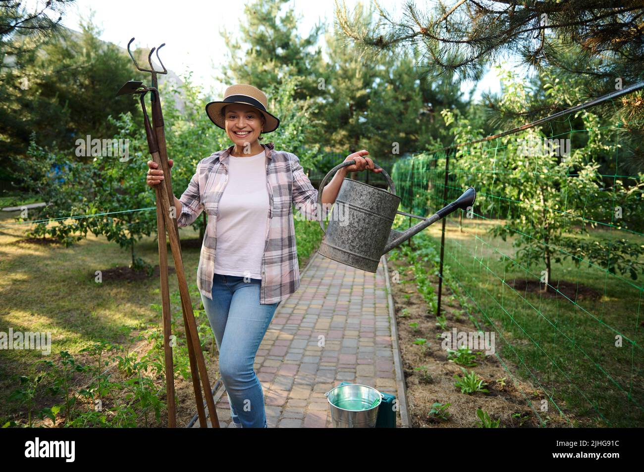 Charming female gardener poses to camera with gardening tools- watering ...