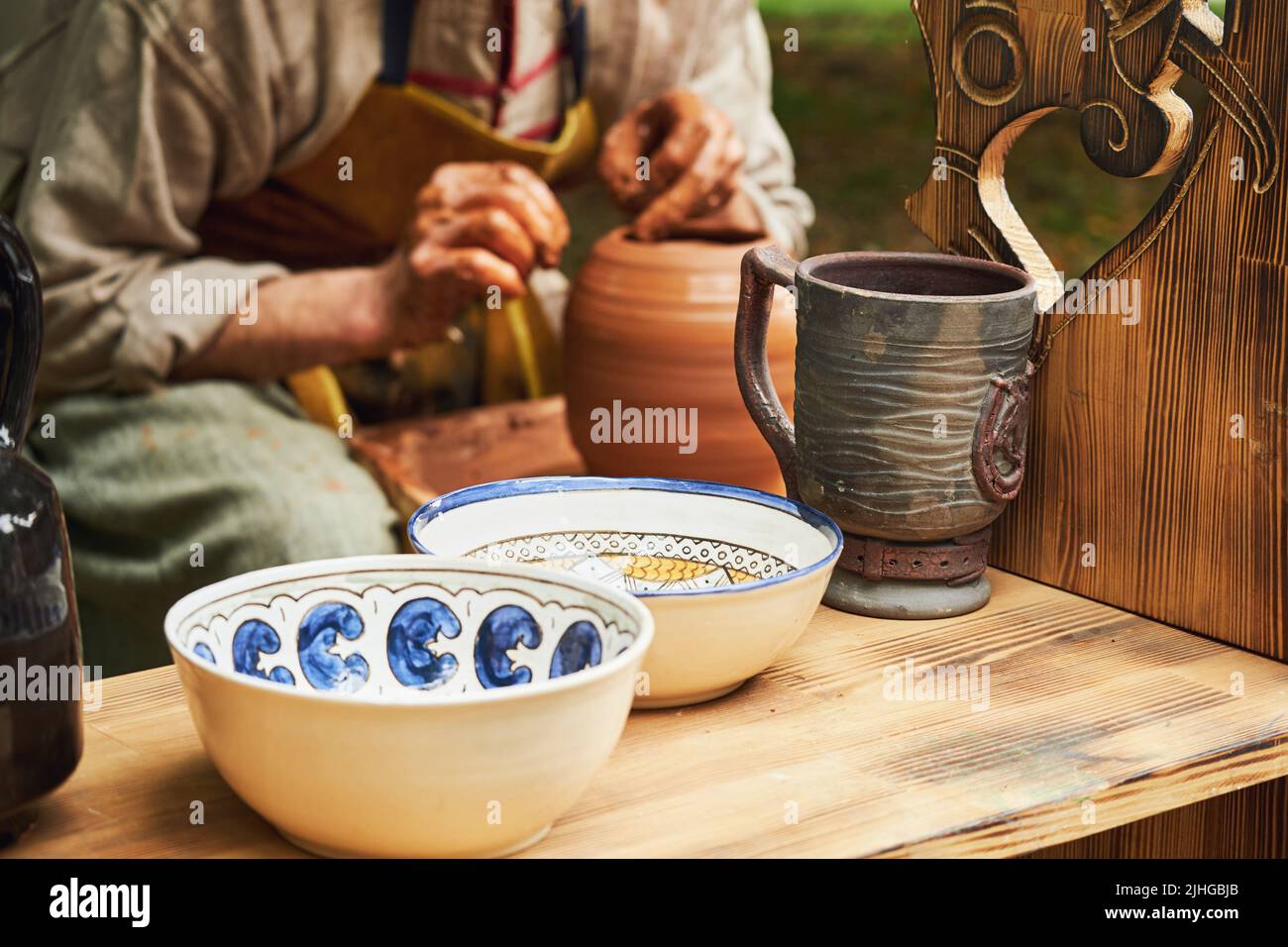 A man in old medieval Byzantine clothes sits behind a vintage potter's ...