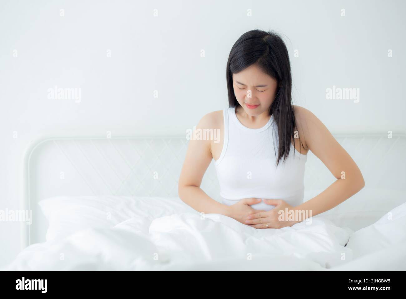 Young asian woman sitting on bed pain stomach or bowel with disease ...