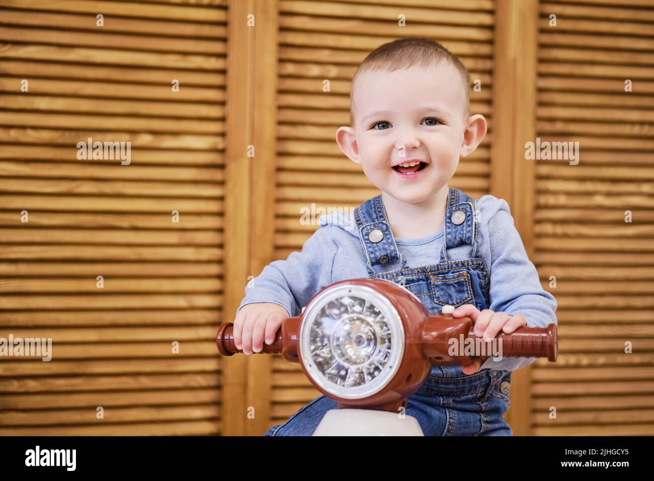 Happy baby boy rides a plastic children motorcycle in the playroom. A ...