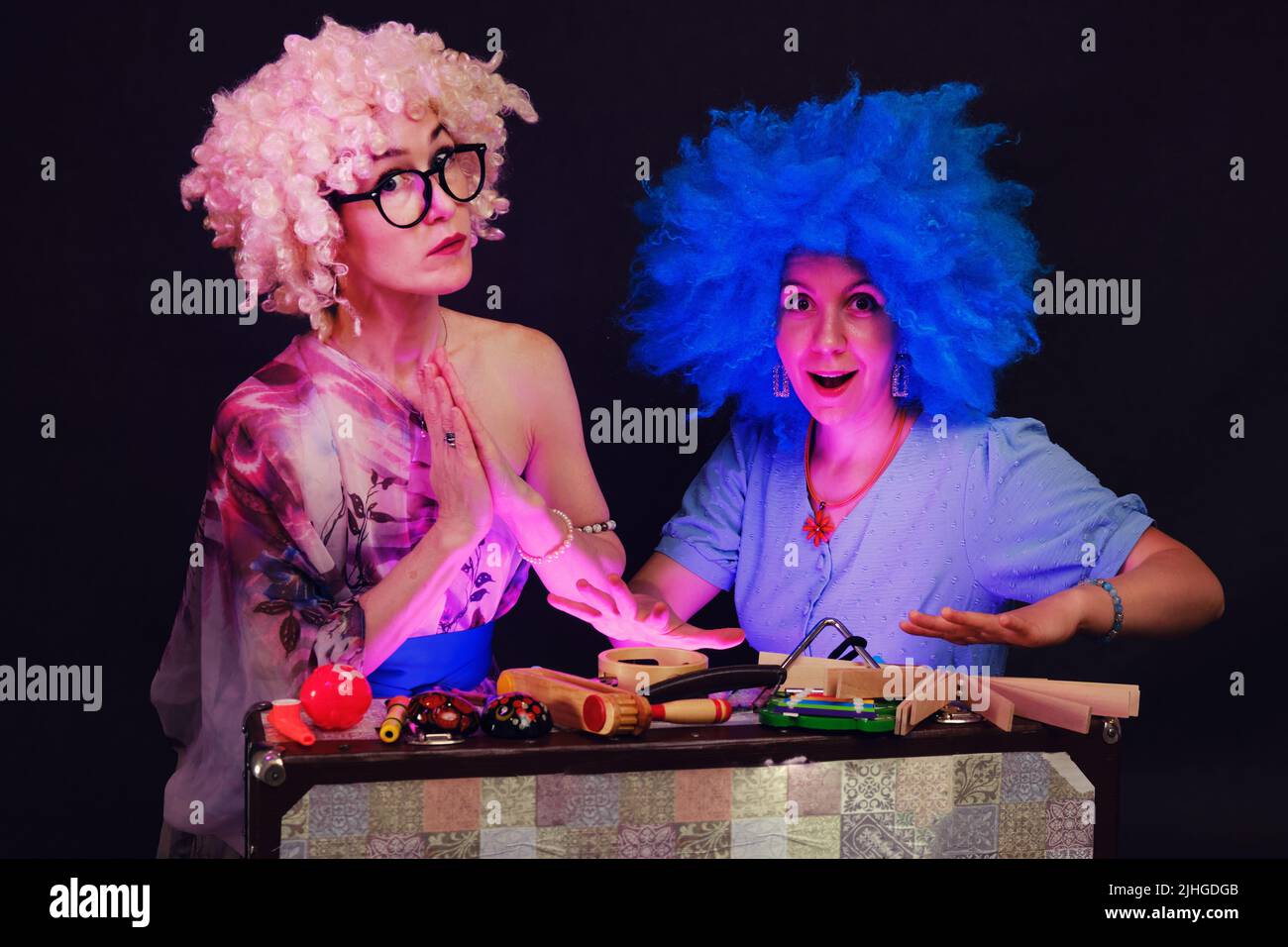 Happy women in funny wigs give a musical performance on a studio black ...