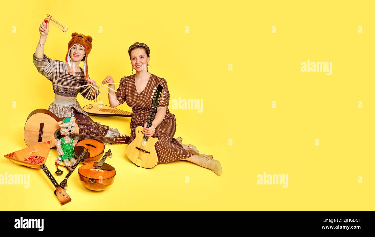 Women musicians in dresses with musical instruments on a yellow studio ...