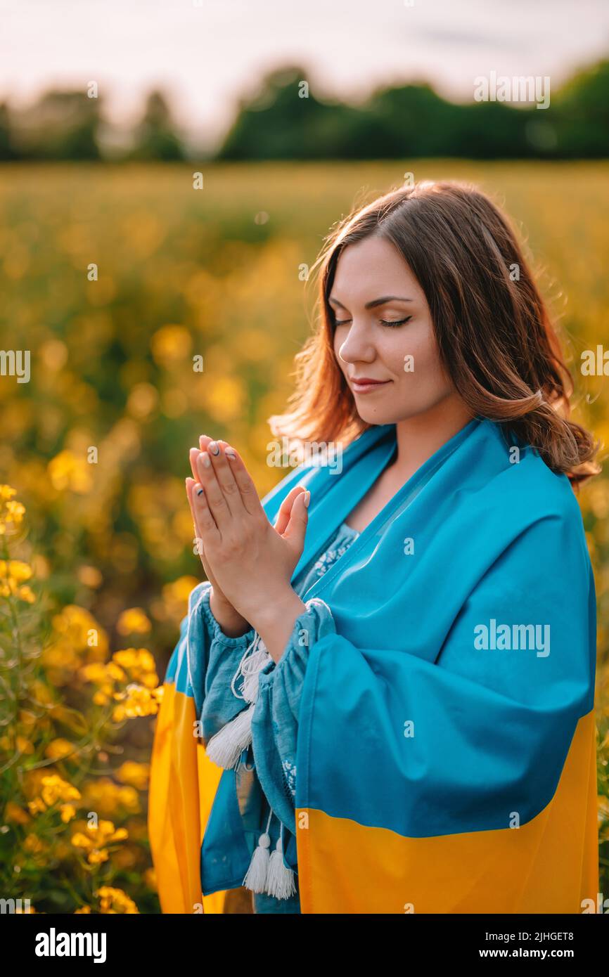 Ukrainian patriot woman praying with national flag in canola yellow ...