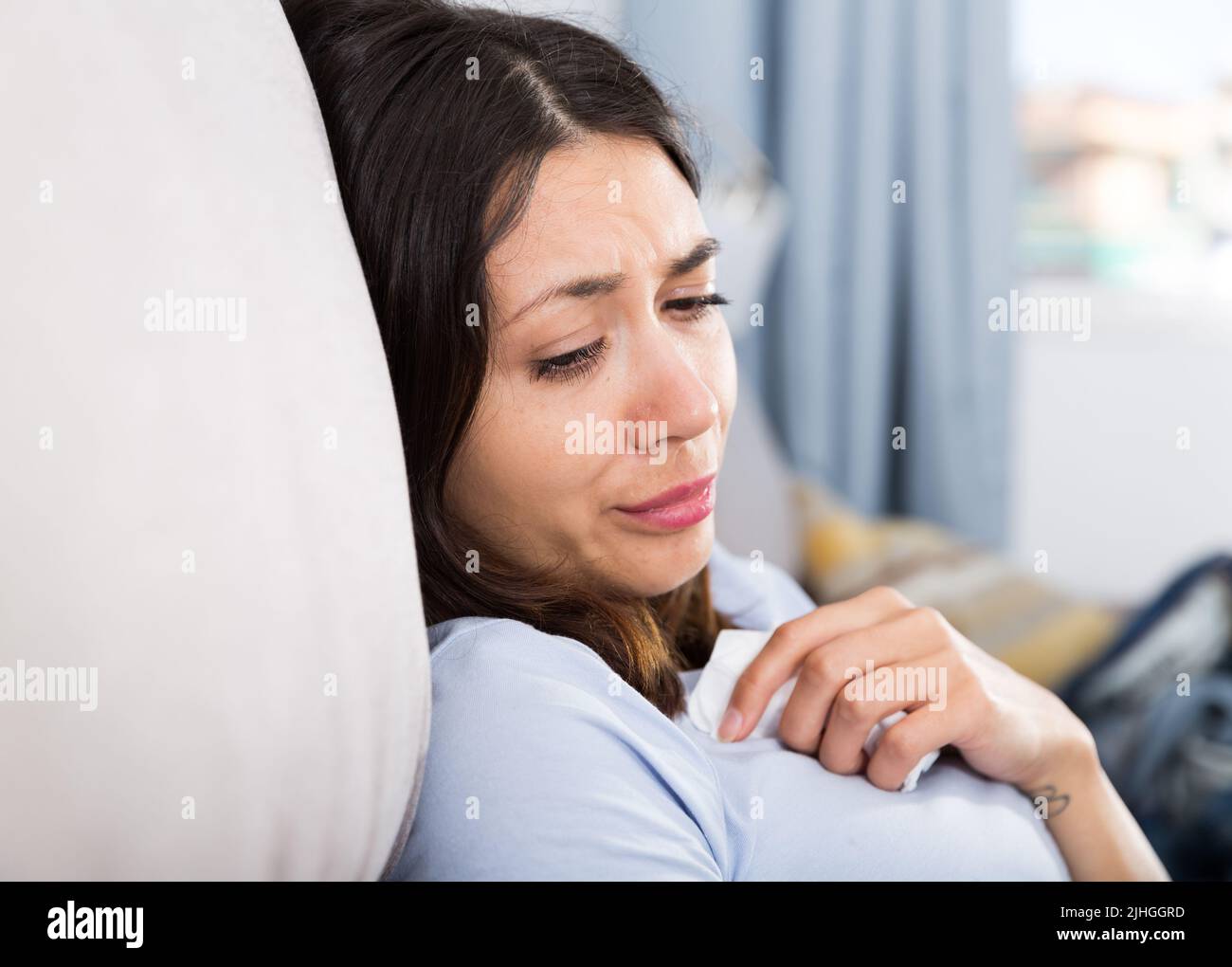 Sad young woman thinking on sofa in home interior Stock Photo - Alamy