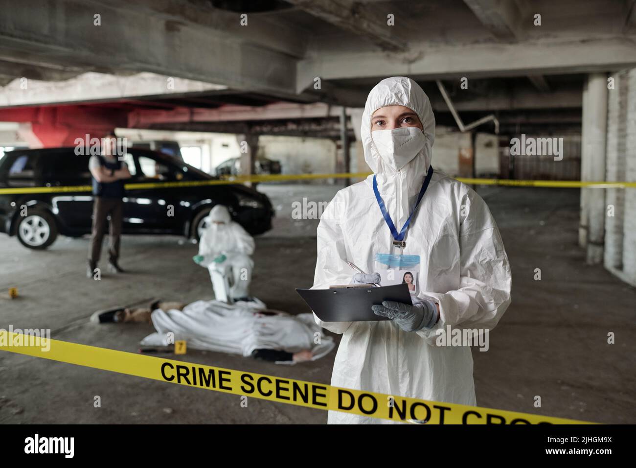 Young female crime scene investigator in protective coveralls making ...