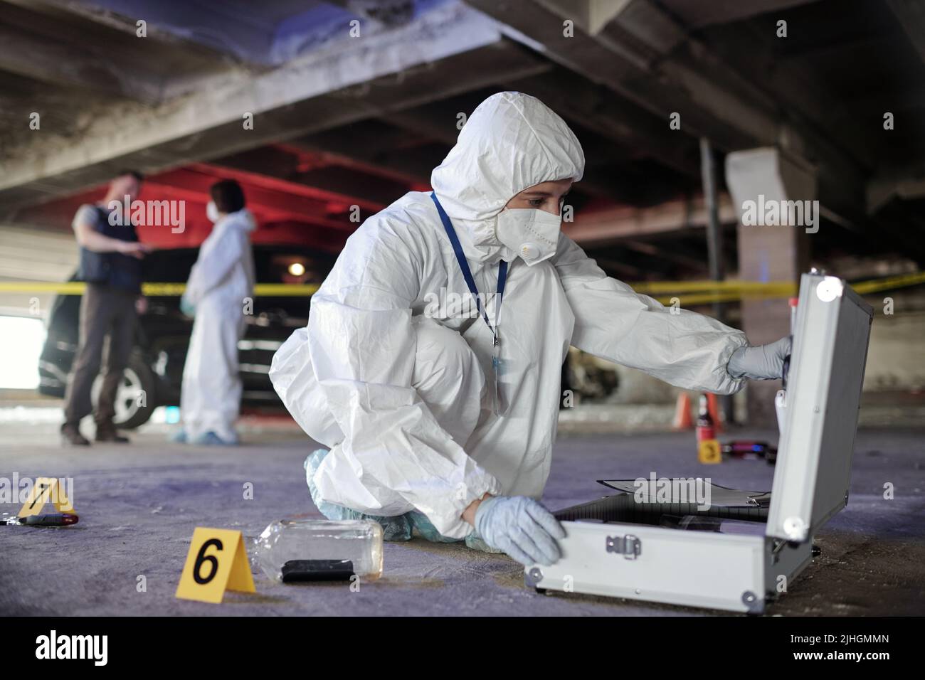 Young female criminological expert in coveralls opening briefcase with ...