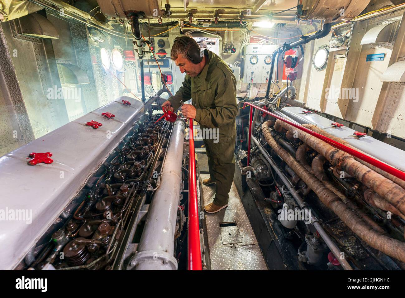 Man, engineer, standing between two large diesel engines, while oiling ...