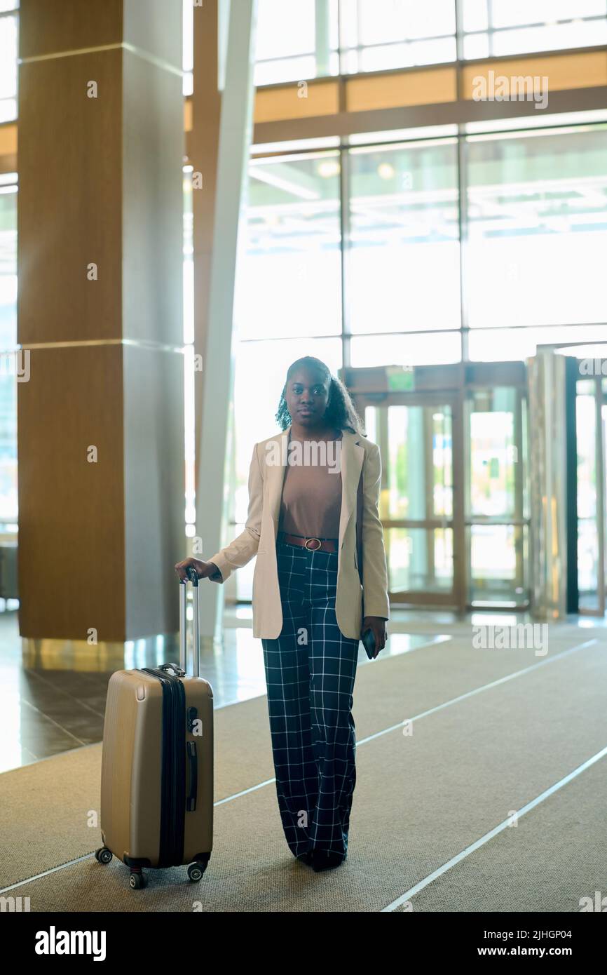 Young serious black woman in smart casualwear holding by handle of ...