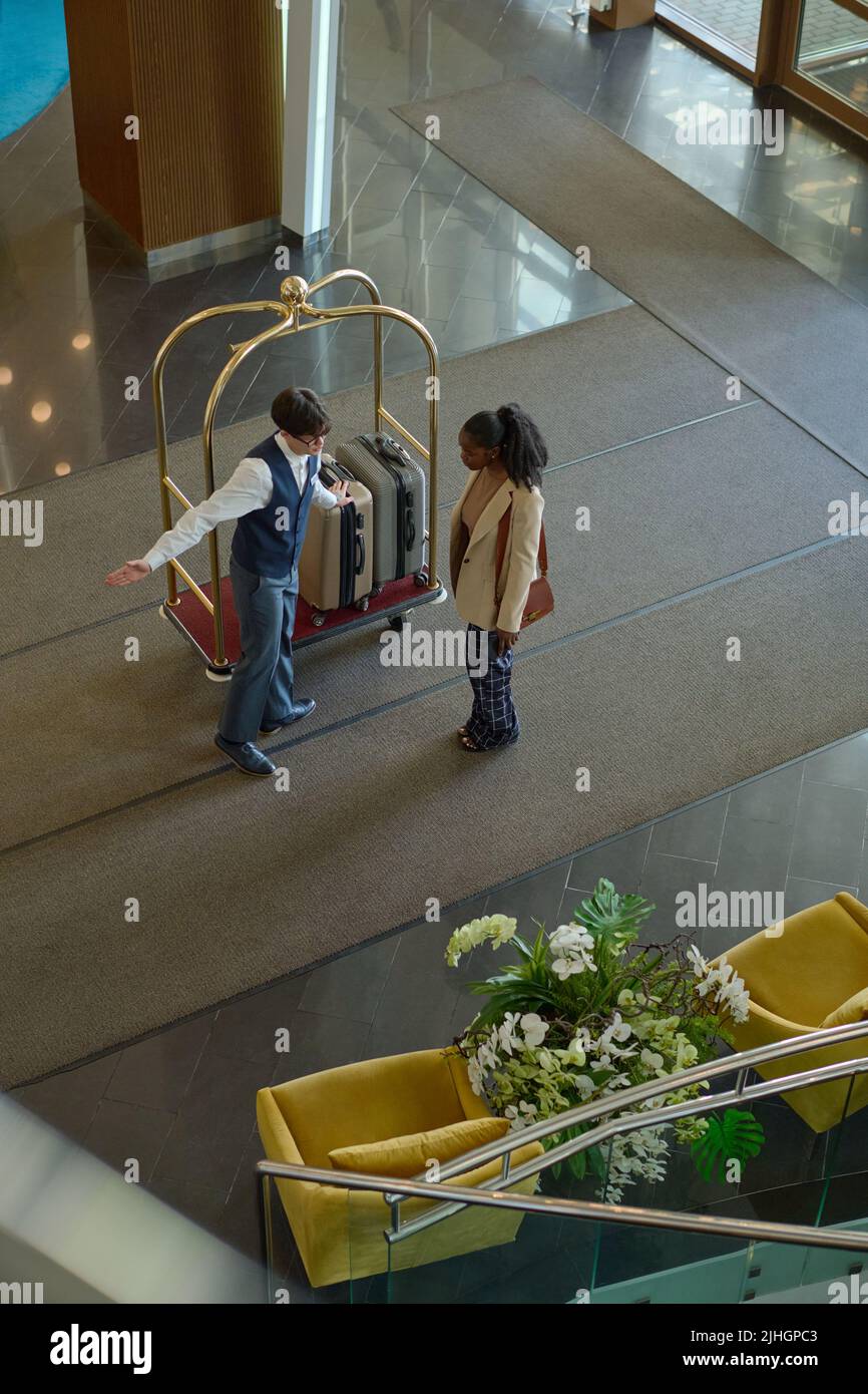 Young man in bellboy uniform showing way to hotel room to African ...