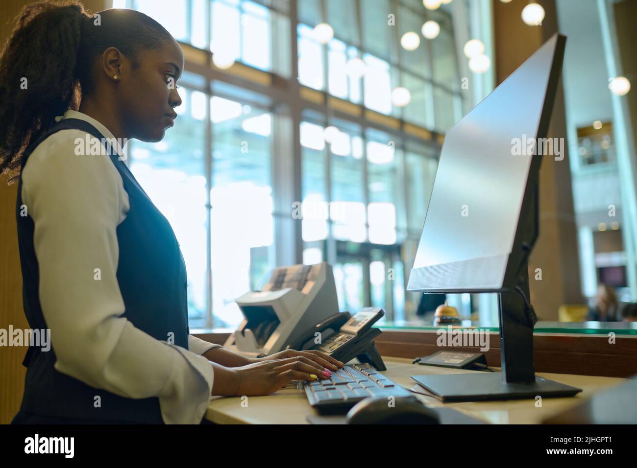 Side view of young black woman in uniform looking at computer screen ...