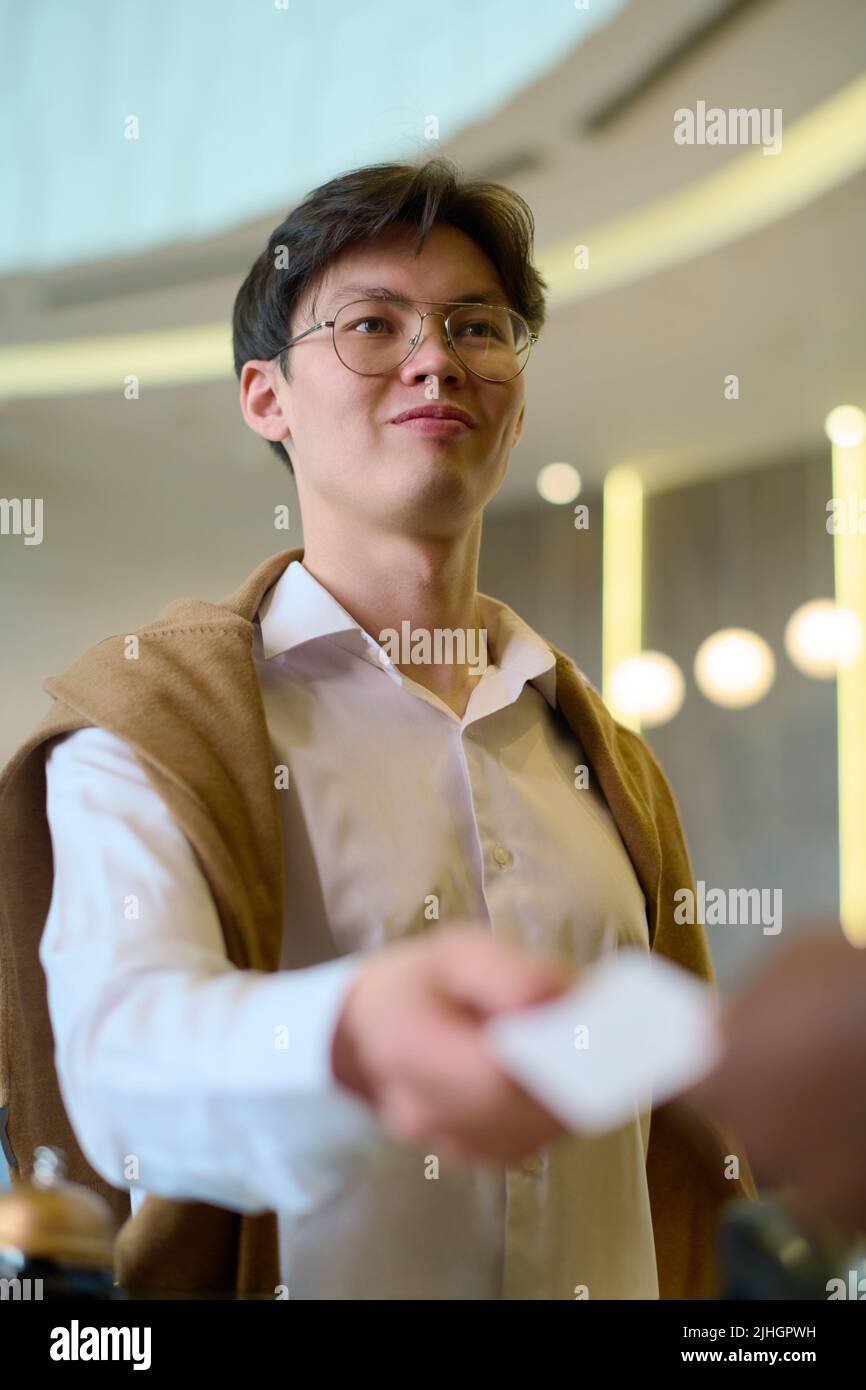 Asian guy in eyeglasses and white shirt passing keycard to receptionist ...