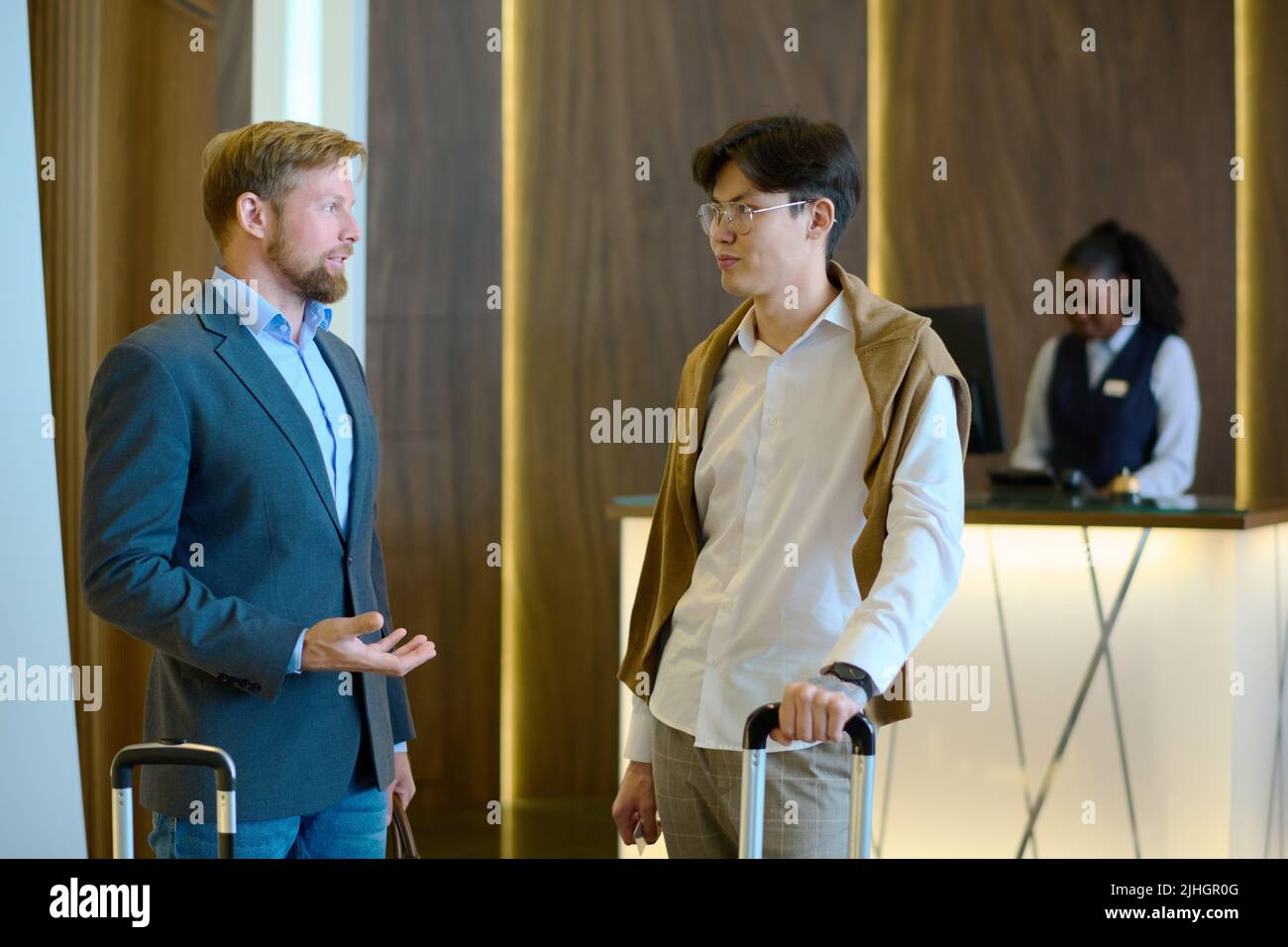 Two young intercultural businessmen with suitcase having discussion in ...