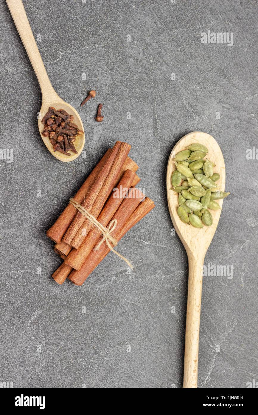 Bunch of cinnamon sticks on black. Cardamom and cloves in wooden spoons ...