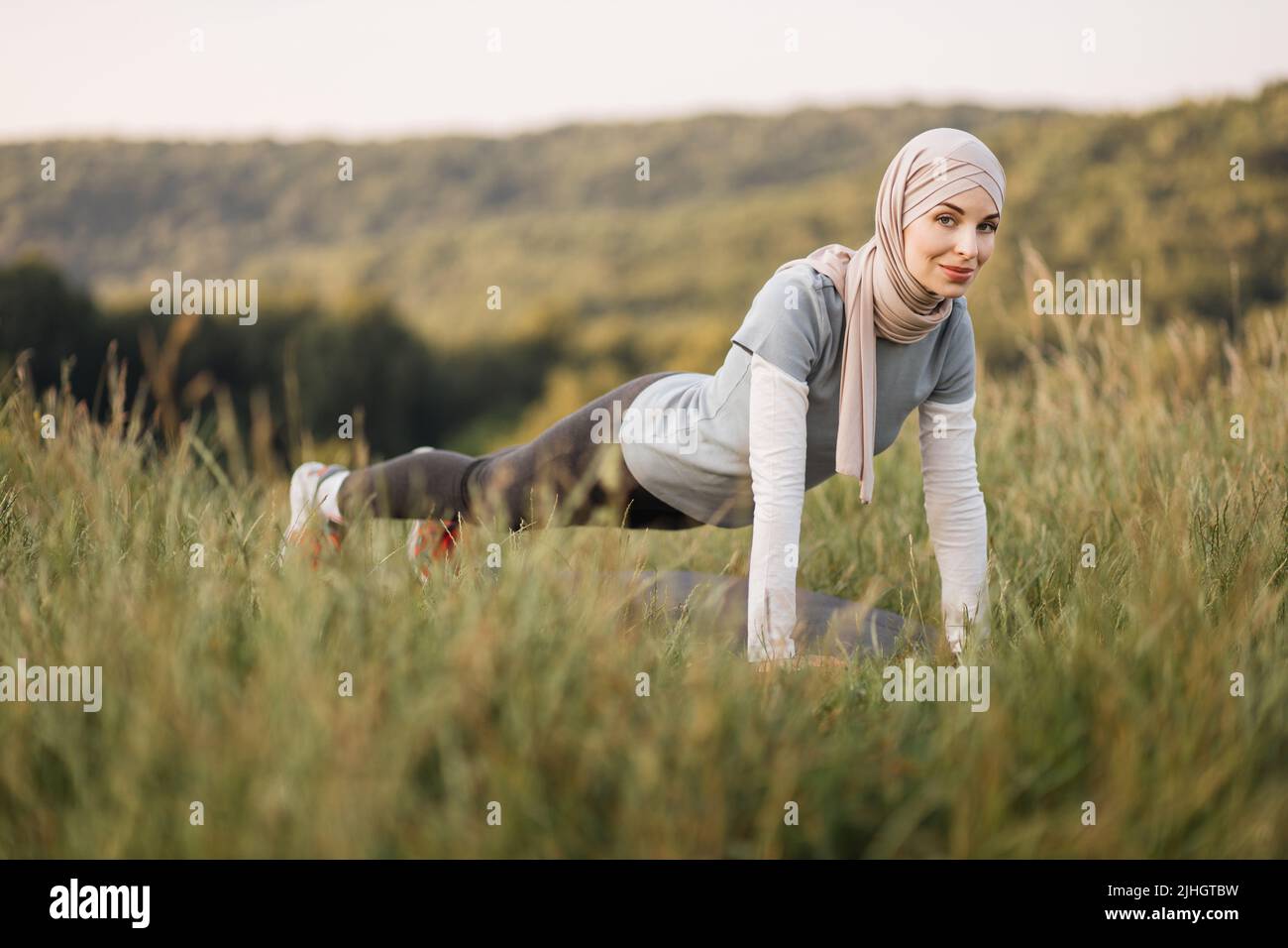 Young muslim woman in hijab and sportswear standing in plank position ...