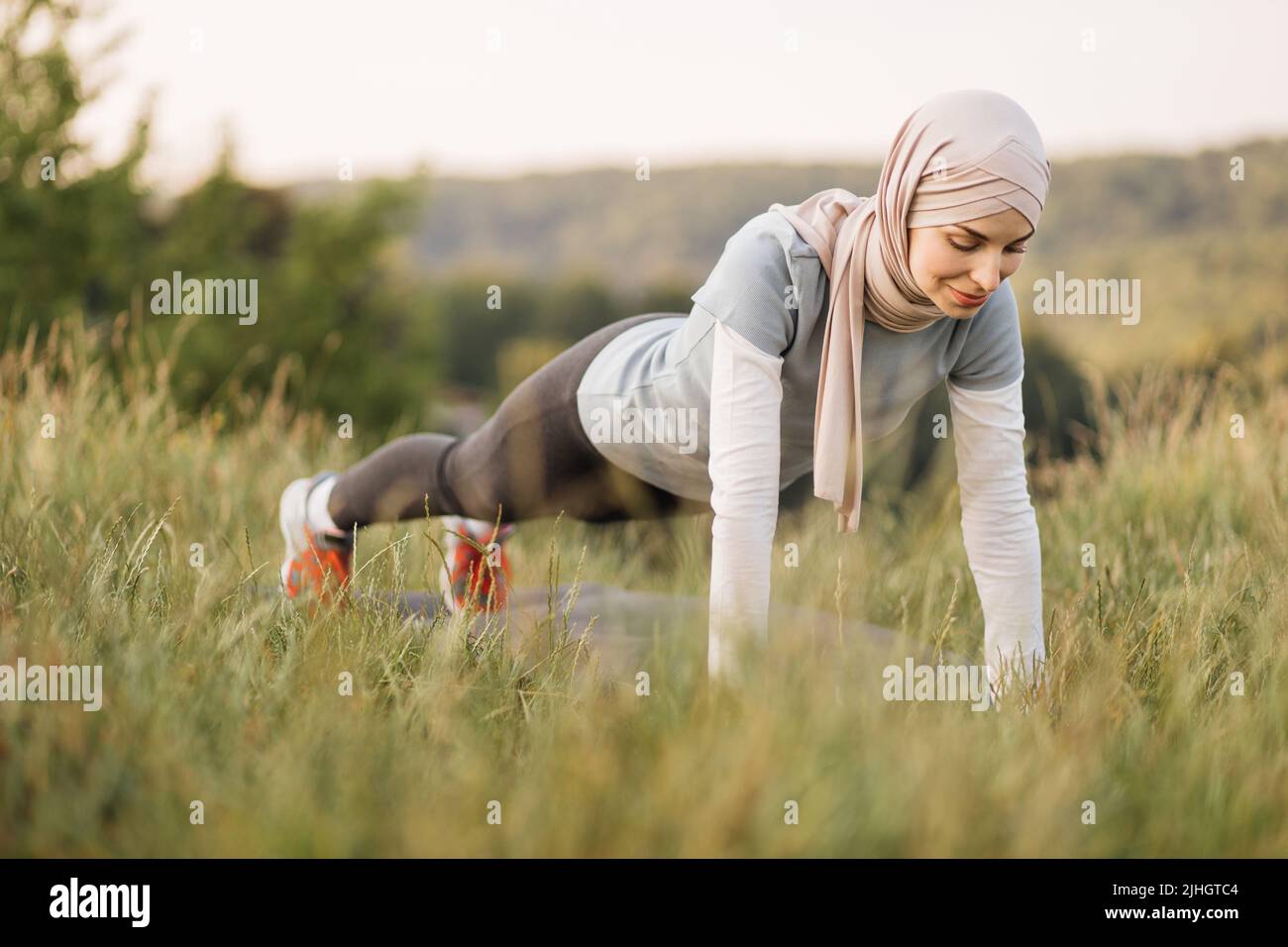 Portrait of attractive young Muslim woman smiling and doing plank ...