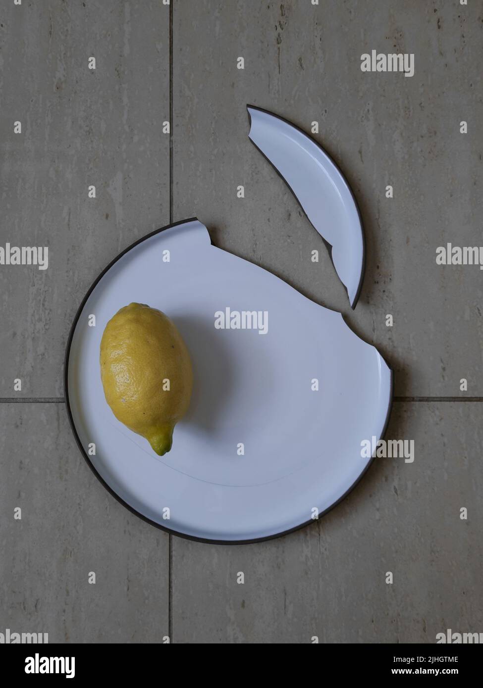Cracked dining plate lays on a tile. Yellow lemon on a broken ceramic ...