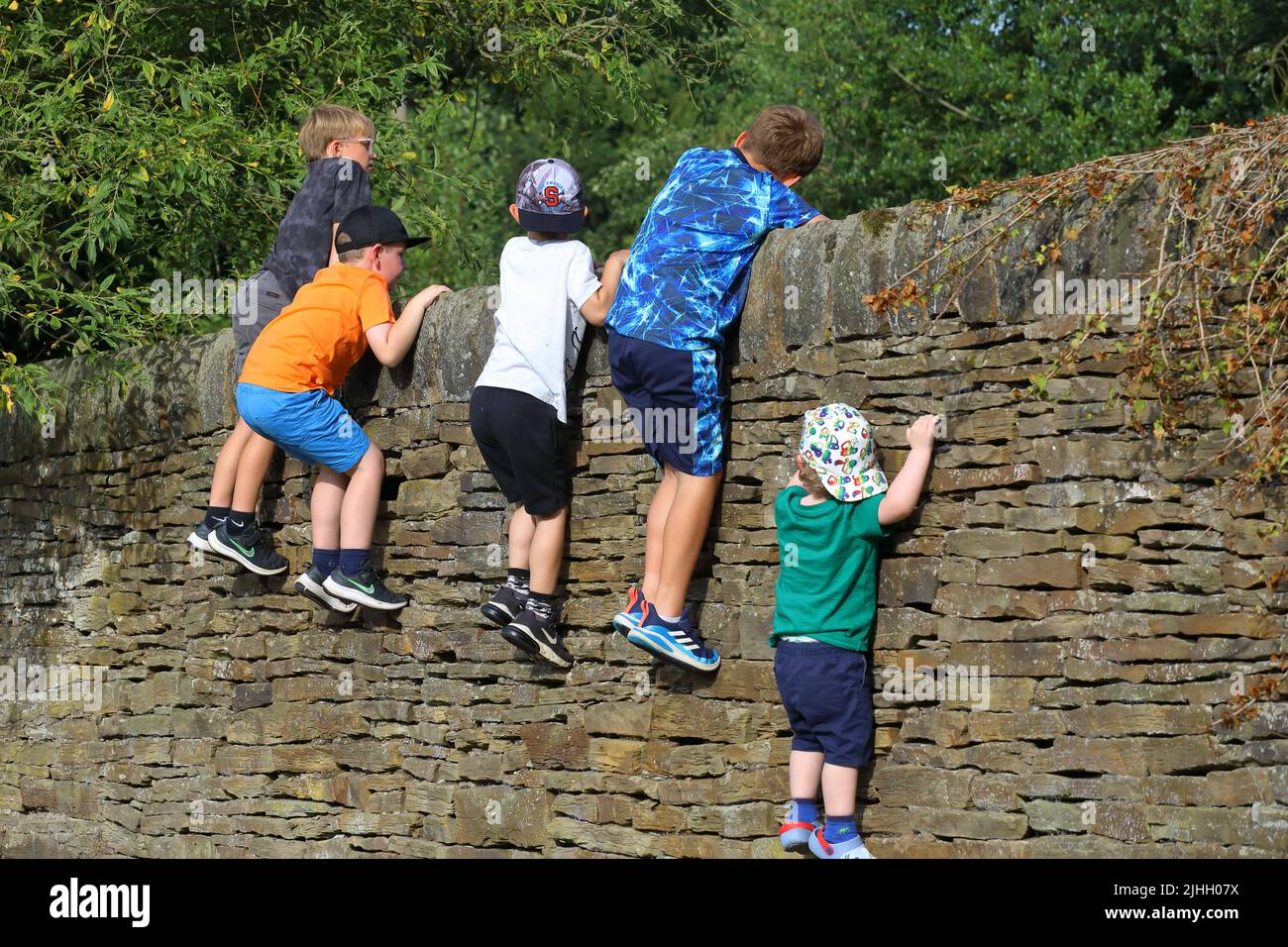 4 young boys looking over a wall. another, the smallest boy looking up ...