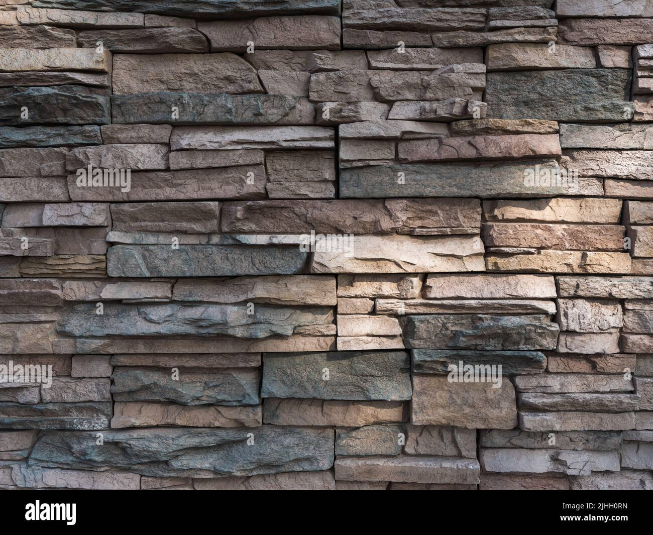 Subtle mottled afternoon sunlight on stacked narrow fieldstone wall ...