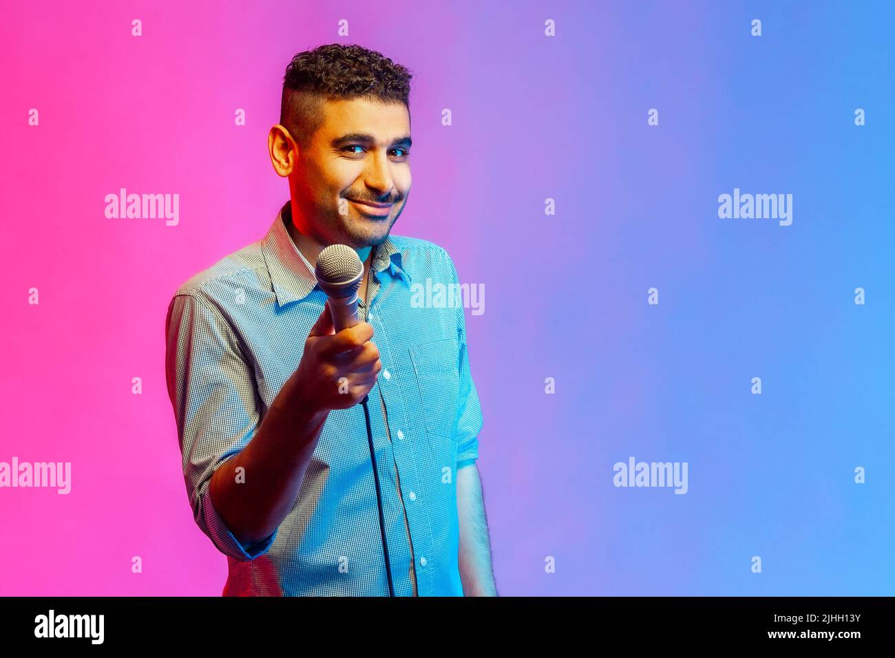 Portrait of man in shirt posing with microphone in hands, offers mic ...