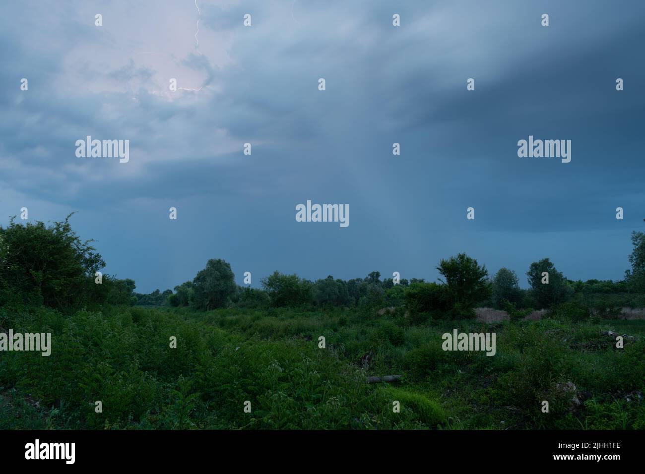 Summer storm with rain and lightning above channel overgrown with grass ...