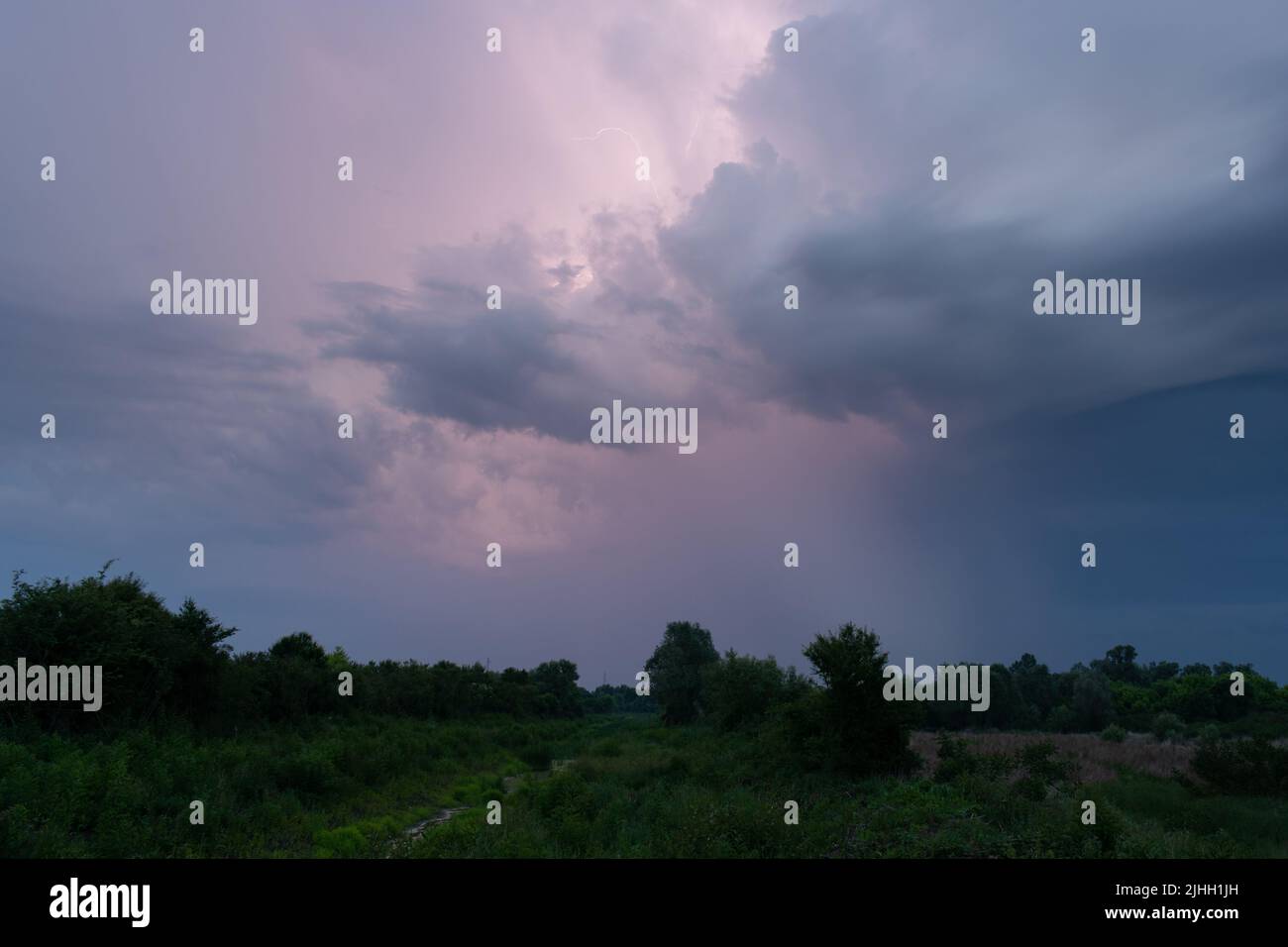 Summer storm with rain and lightning above channel overgrown with grass ...