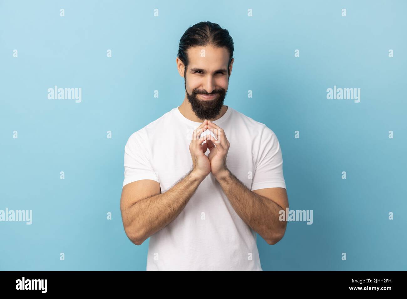 Portrait of devious man with beard wearing white T-shirt smirking and ...