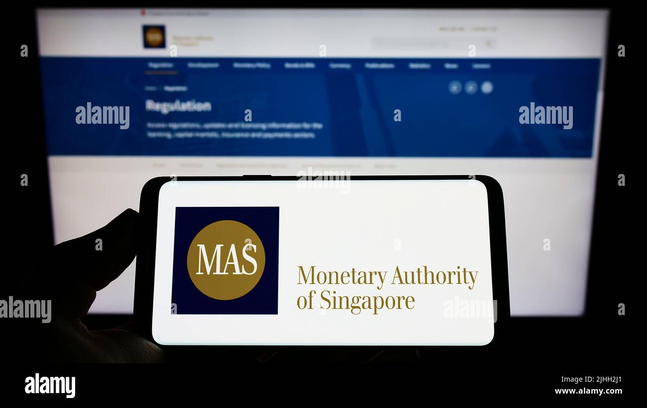 Person holding mobile phone with logo of Monetary Authority of ...
